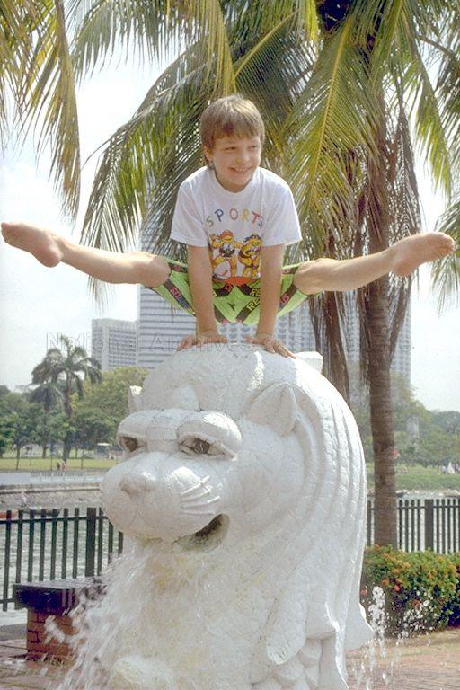 A BOY STRIKING A GYMNASTIC POSE ATOP THE SMALL MERLION AT