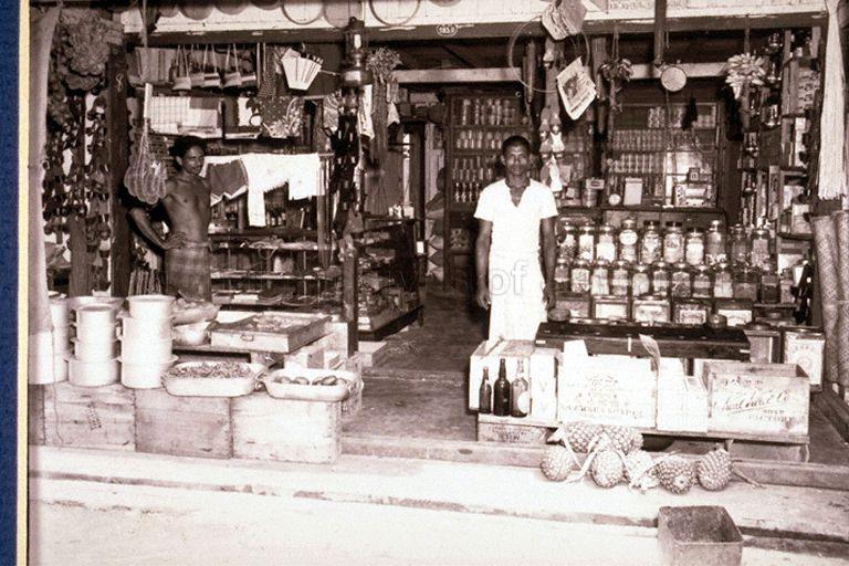 PHOTOGRAPH OF A SHOPKEEPER IN HIS PROVISION SHOP IN JALAN
