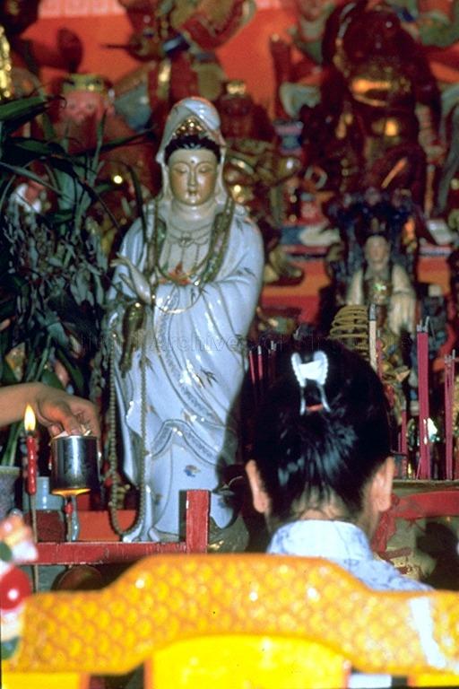 Medium (tangki) seated back to camera, facing statue of