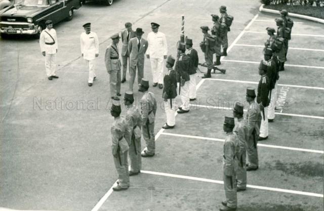 Governor Sir William Goode in a suit and hat arriving at the